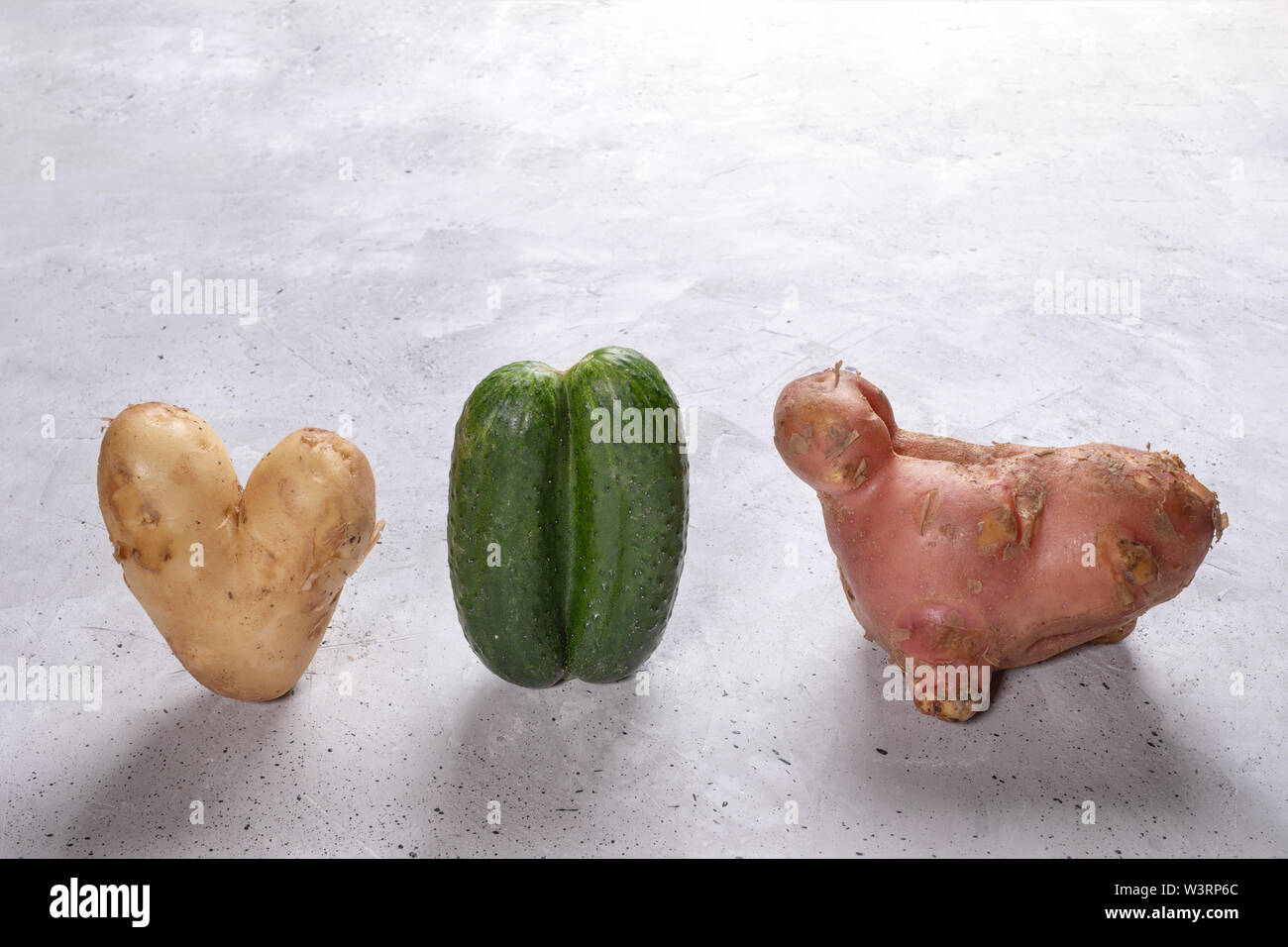 Three ugly vegetables: potato and cucumber on grey concrete background ...