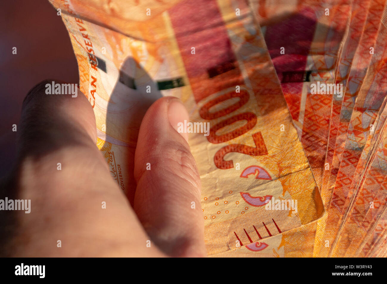A close up view of a hand holding two hundred south african notes in a ...