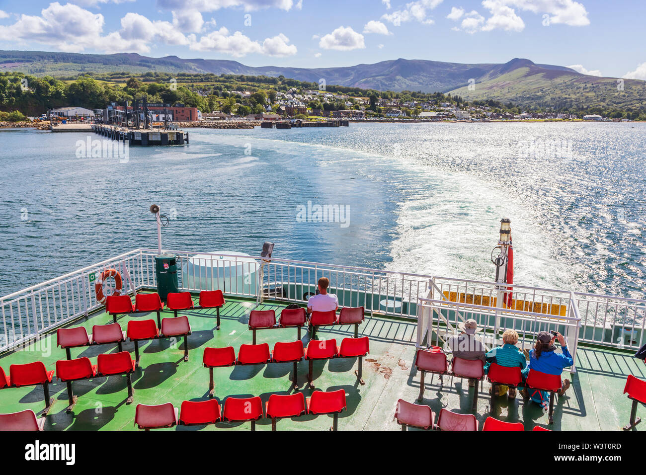 Passengers sitting at the stern of a Caledonian MacBrayne ferry leaving ...