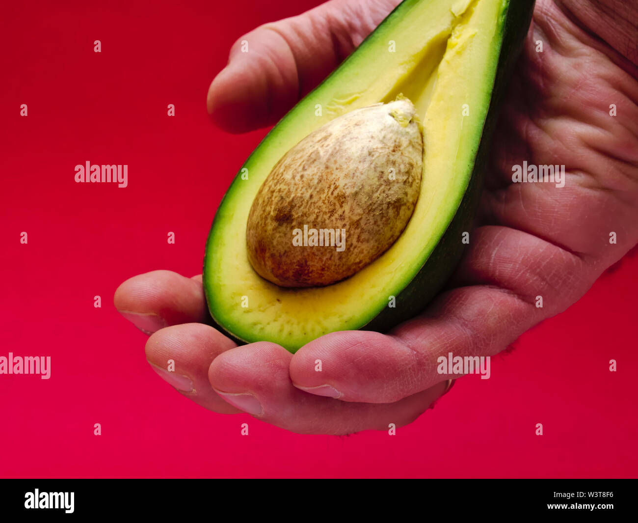 Man hand offering a half cut avocado with seed on magenta pink ...