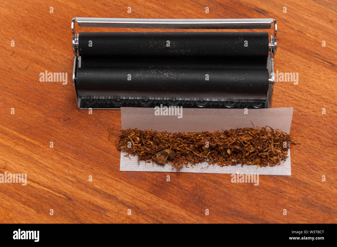 Hand rolling cigarettes machine on the wood and tobacco on the paper ...