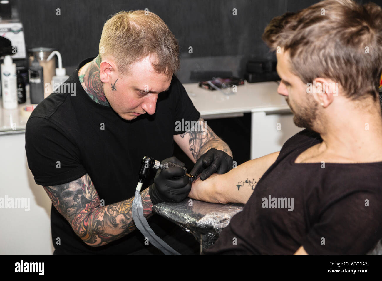Master makes tattoo on arm of man in light studio Stock Photo - Alamy