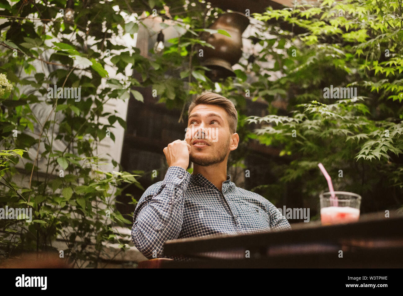Young man sitting in a cafe, drinking coffee and talking on a mobile ...
