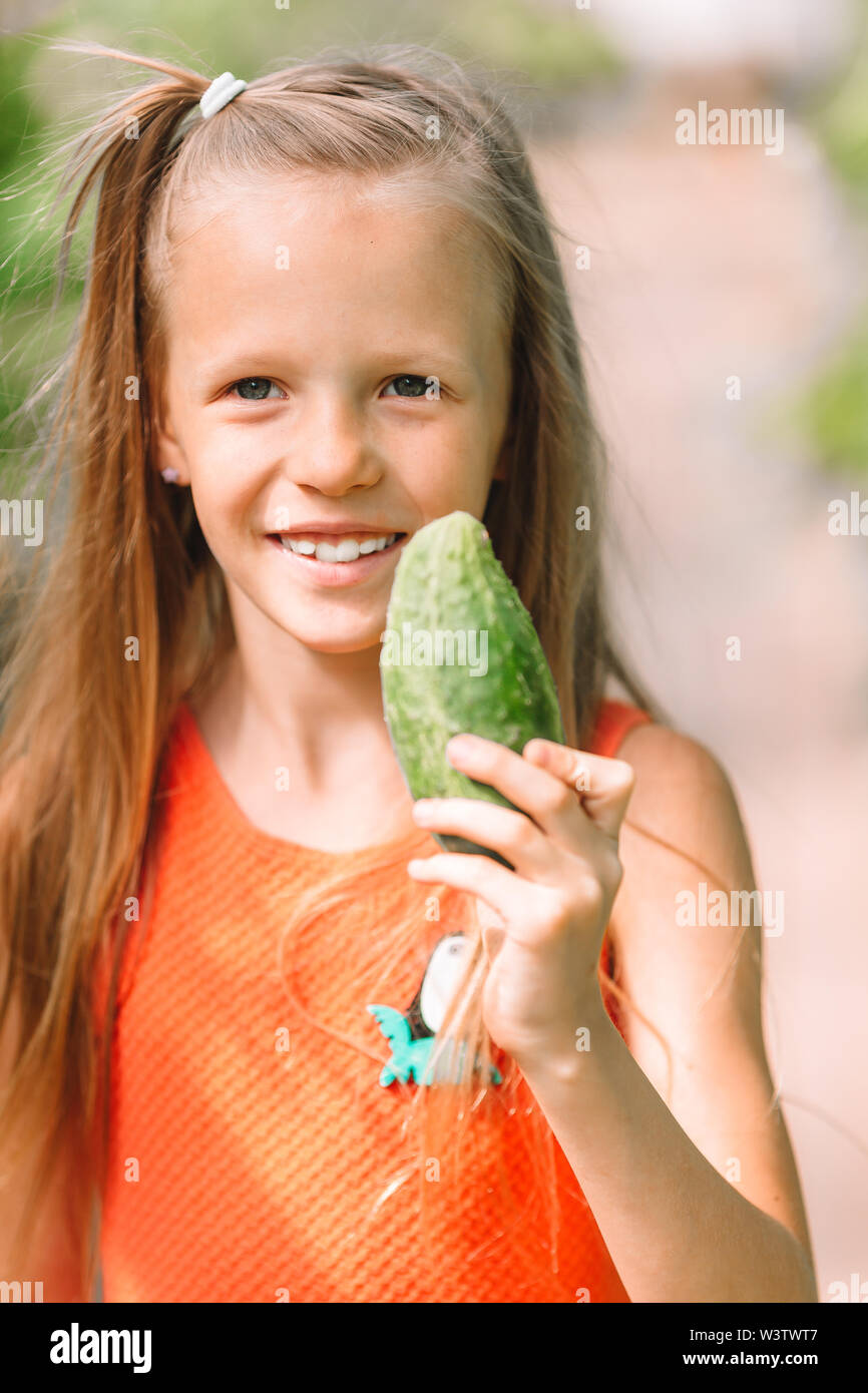 Adorable little girl harvesting cucumbers and tomatoes in greenhouse ...