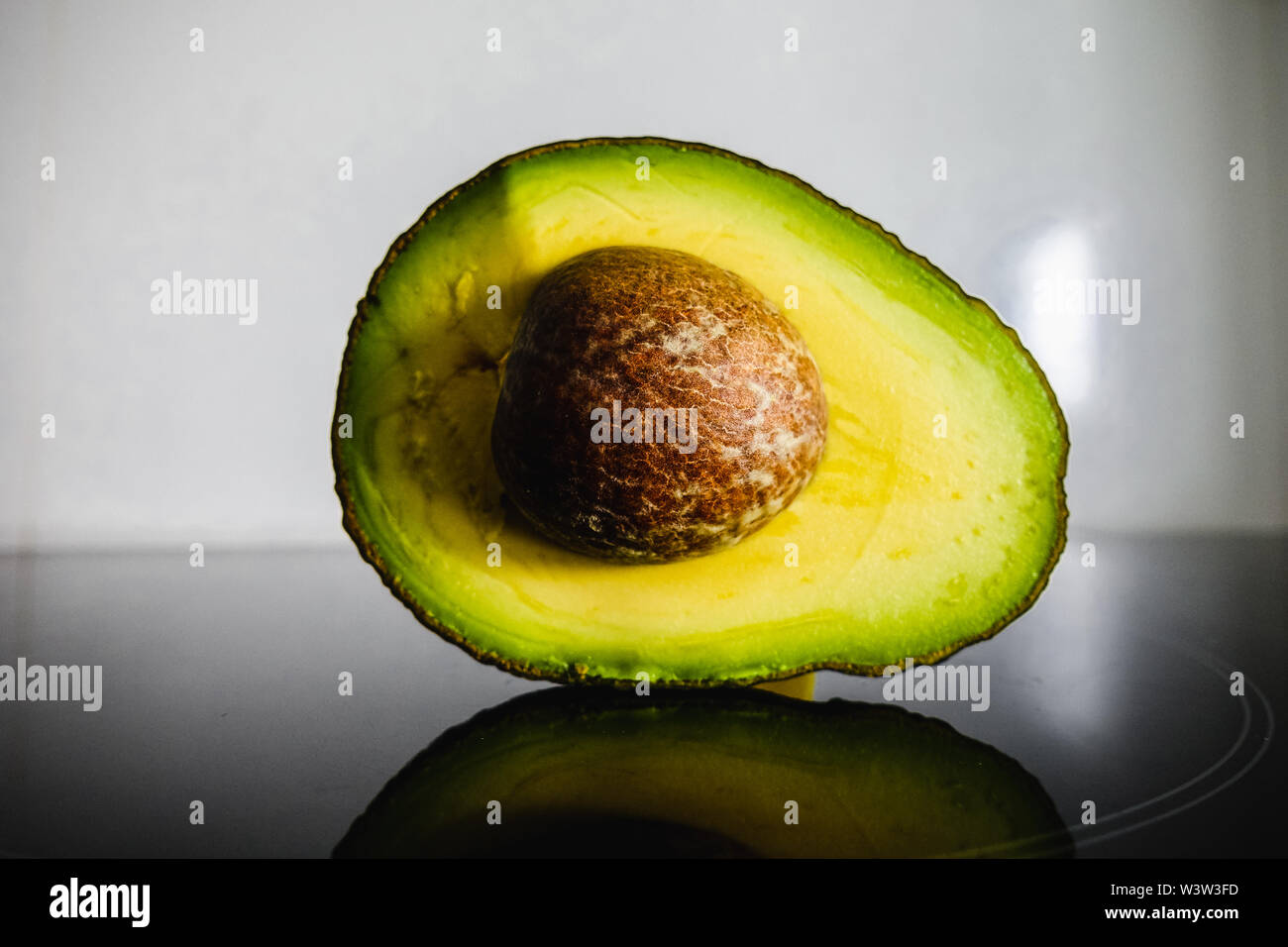 Avocado, cross section, with its reflection in a black surface of a ...