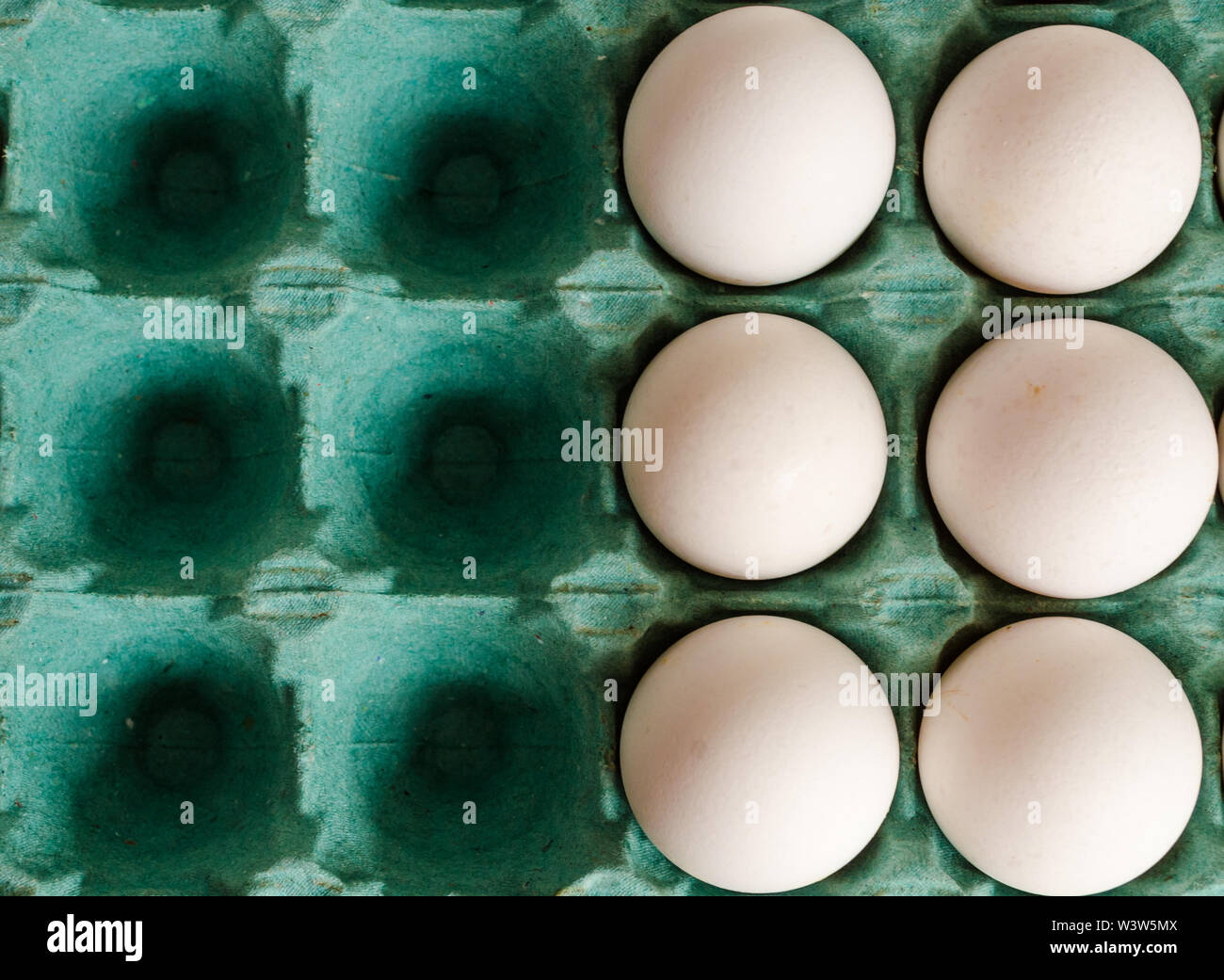 white eggs arranged together to the right side of a green egg carton ...