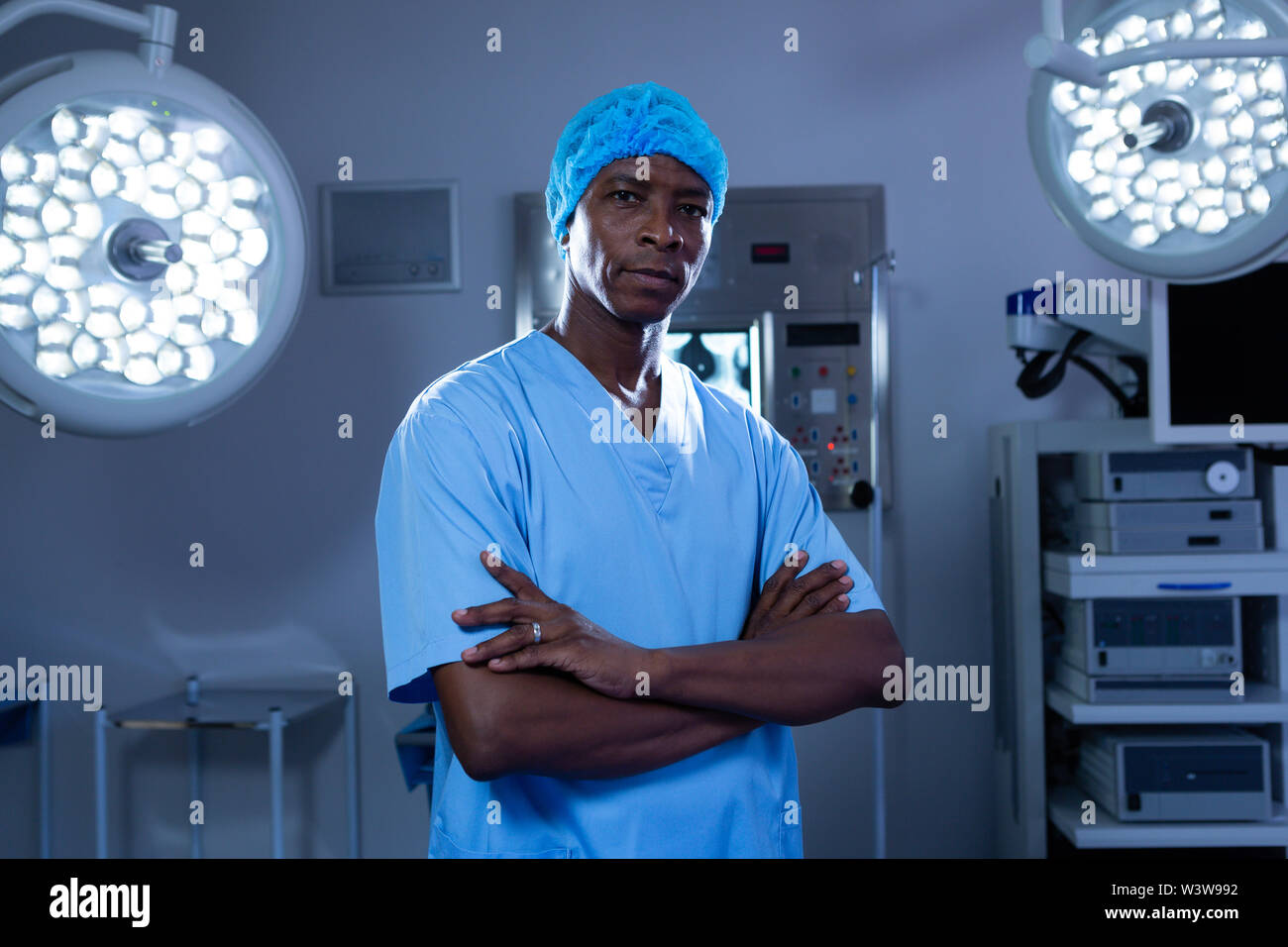 Male surgeon with arms crossed standing in operating room of hospital ...