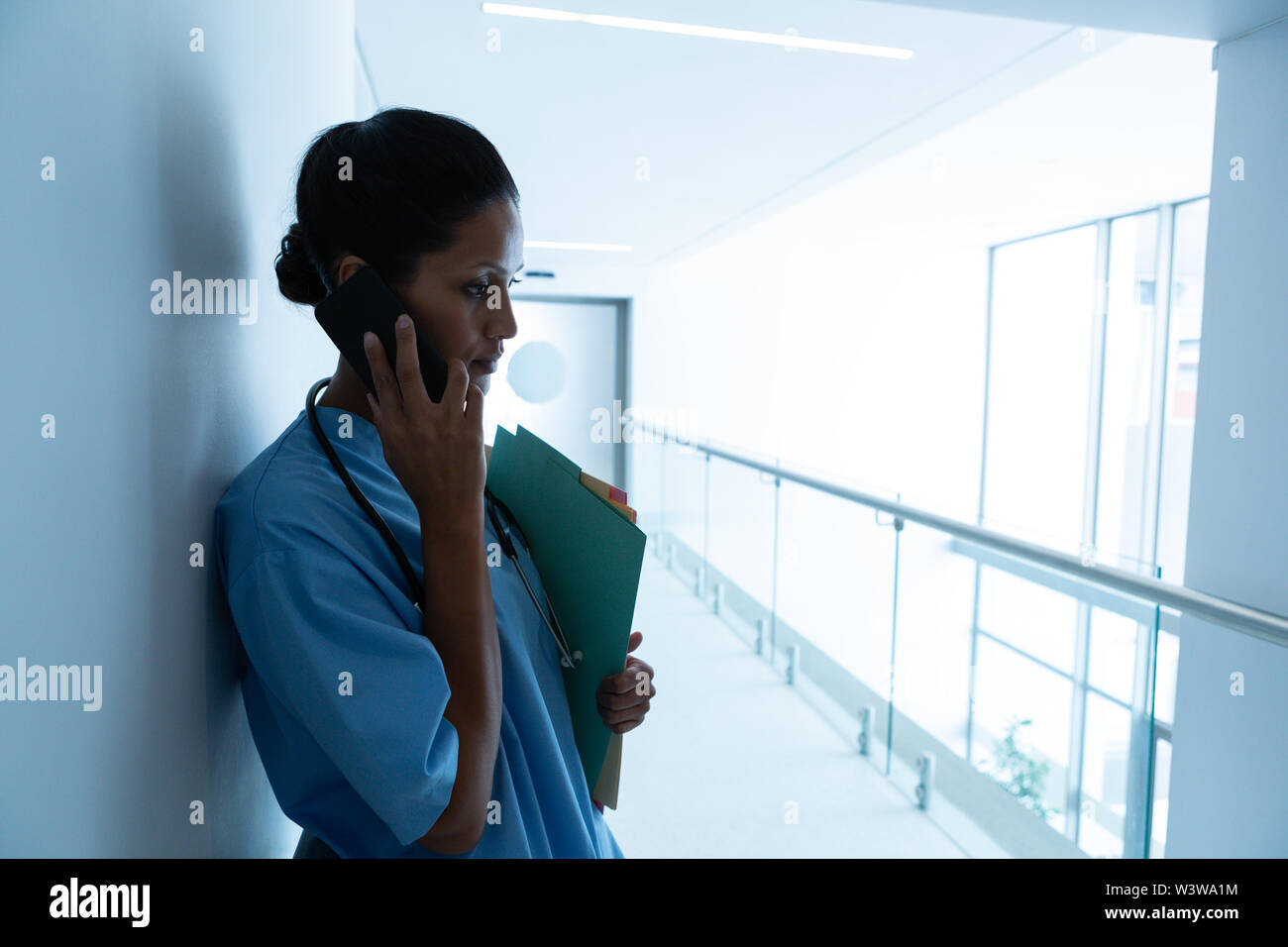 Female surgeon talking on mobile phone while leaning against wall in ...