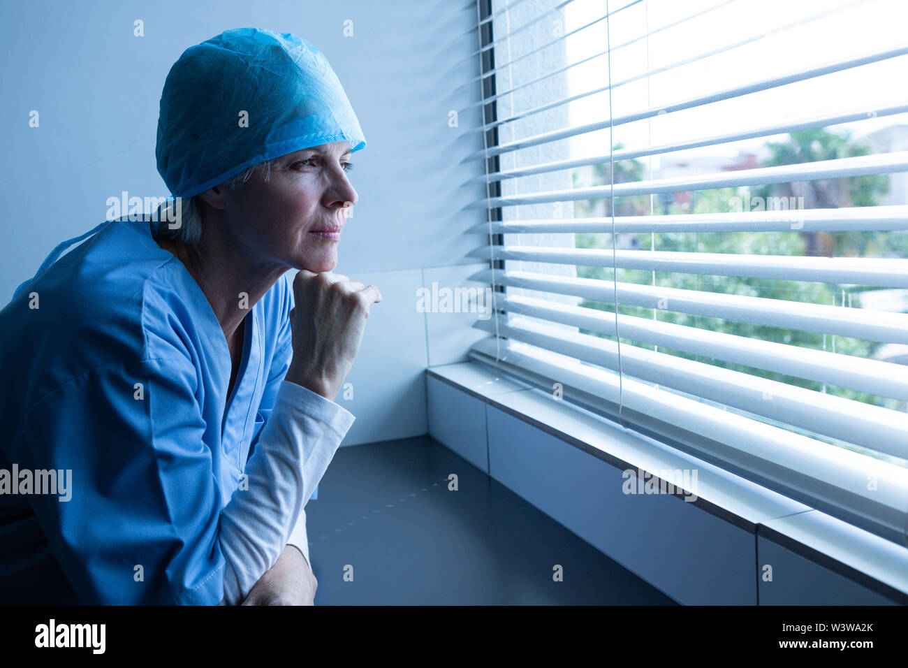 Female surgeon looking through window blinds in the hospital Stock ...