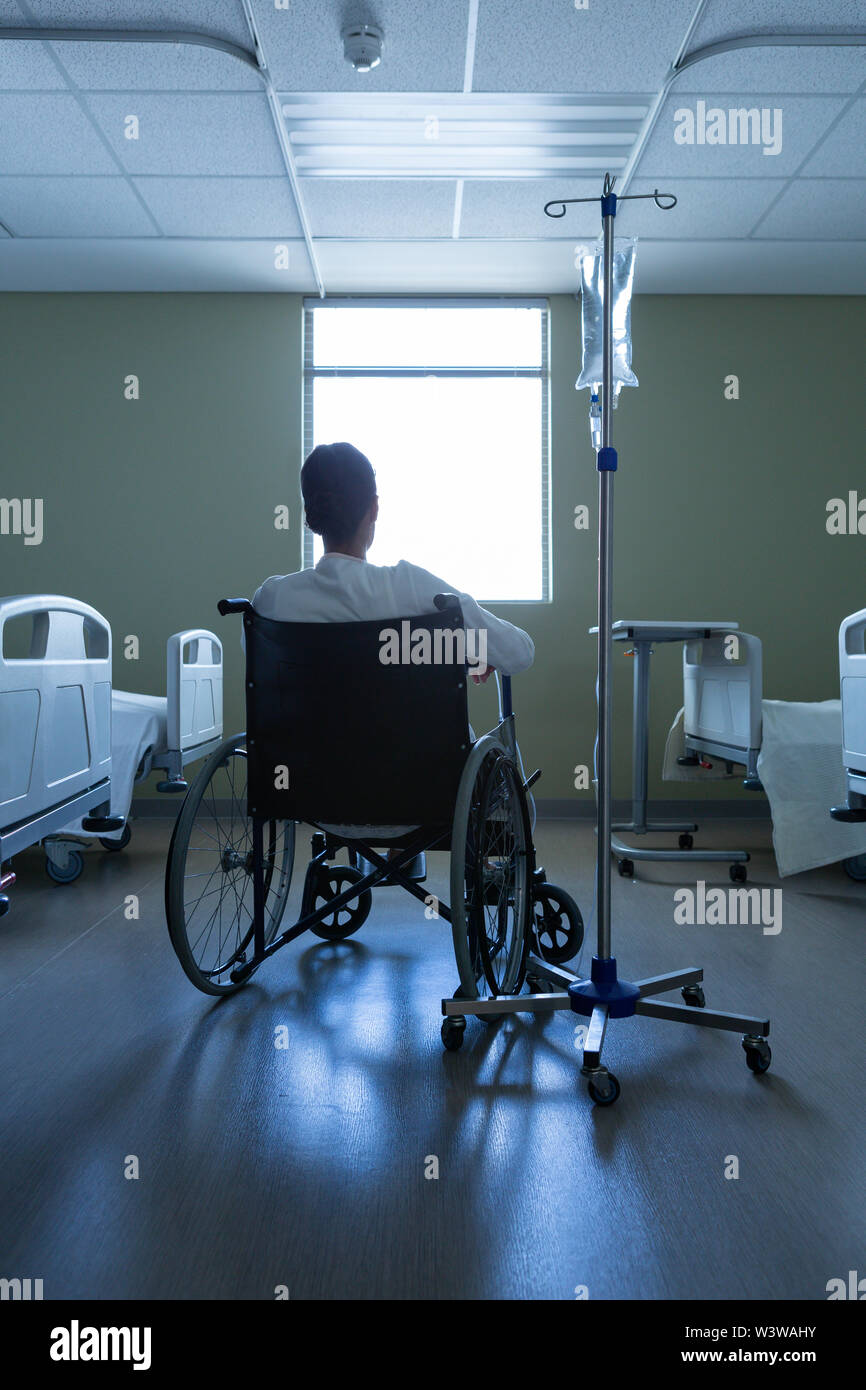 Patient looking through window while sitting in wheelchair in hospital ...
