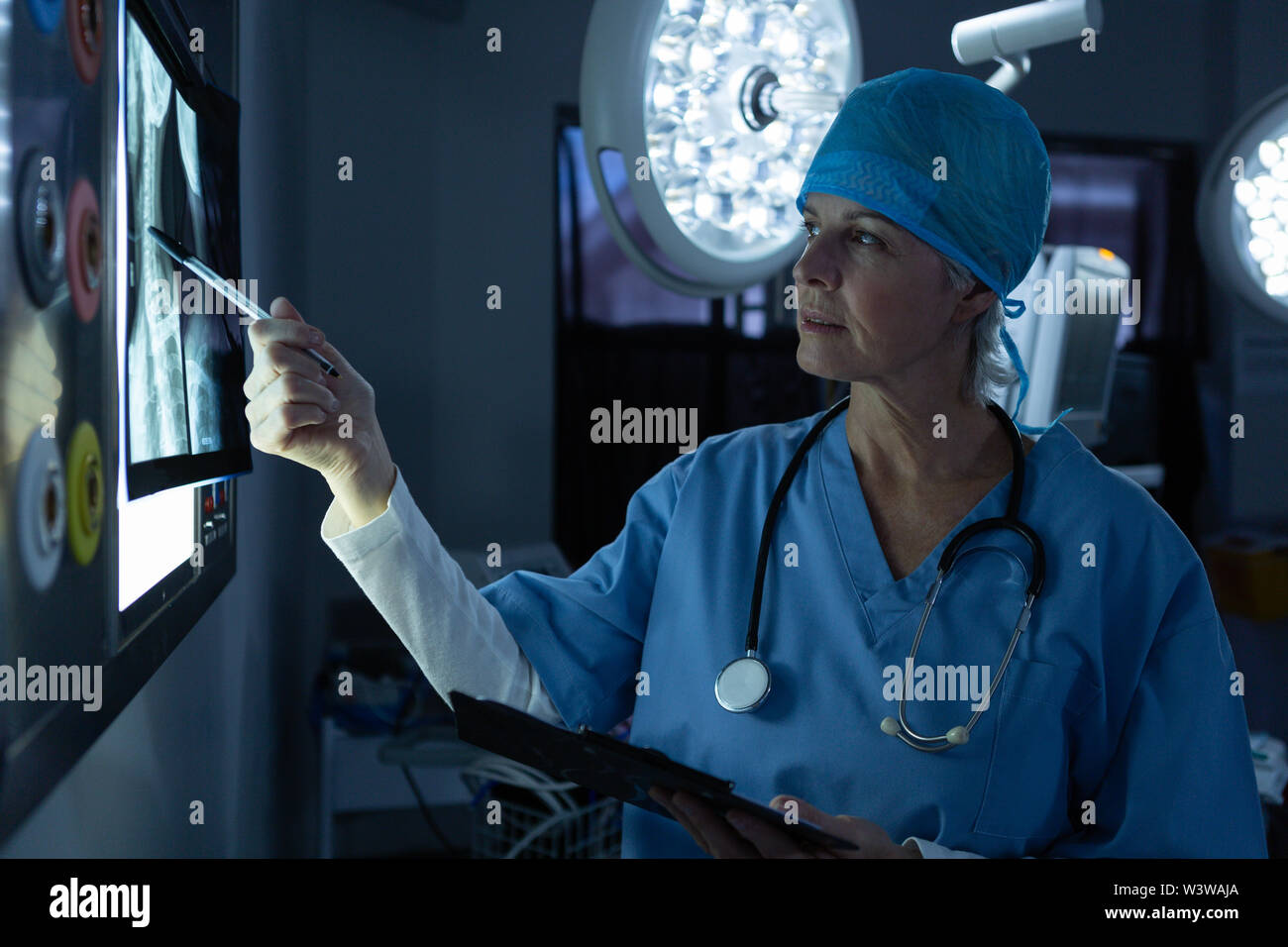 Surgeon examining x-ray while writing on clipboard in operating room of ...