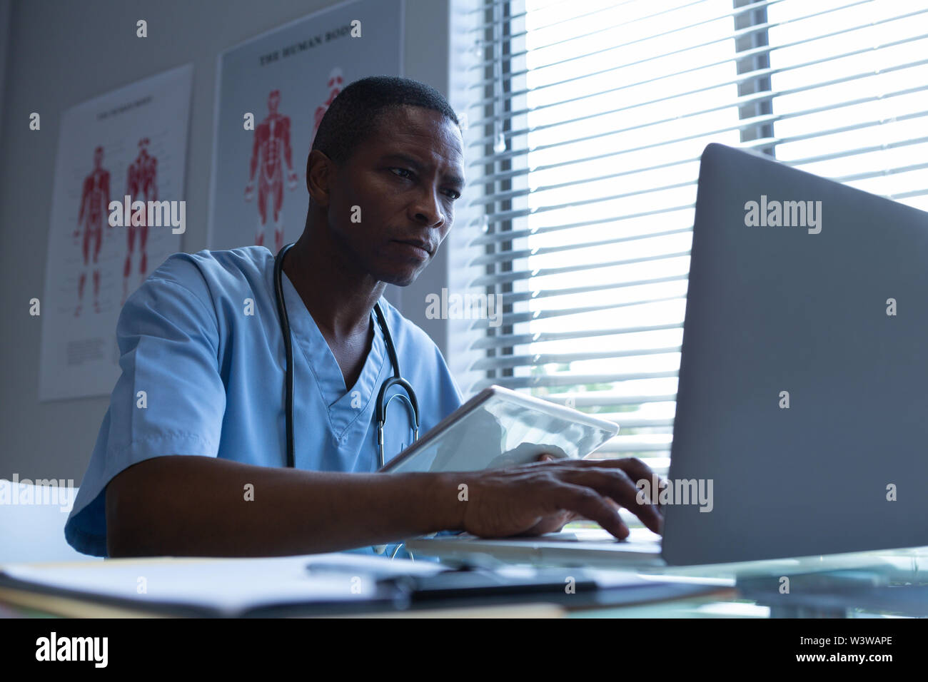 Male surgeon using laptop while holding digital tablet at desk Stock ...