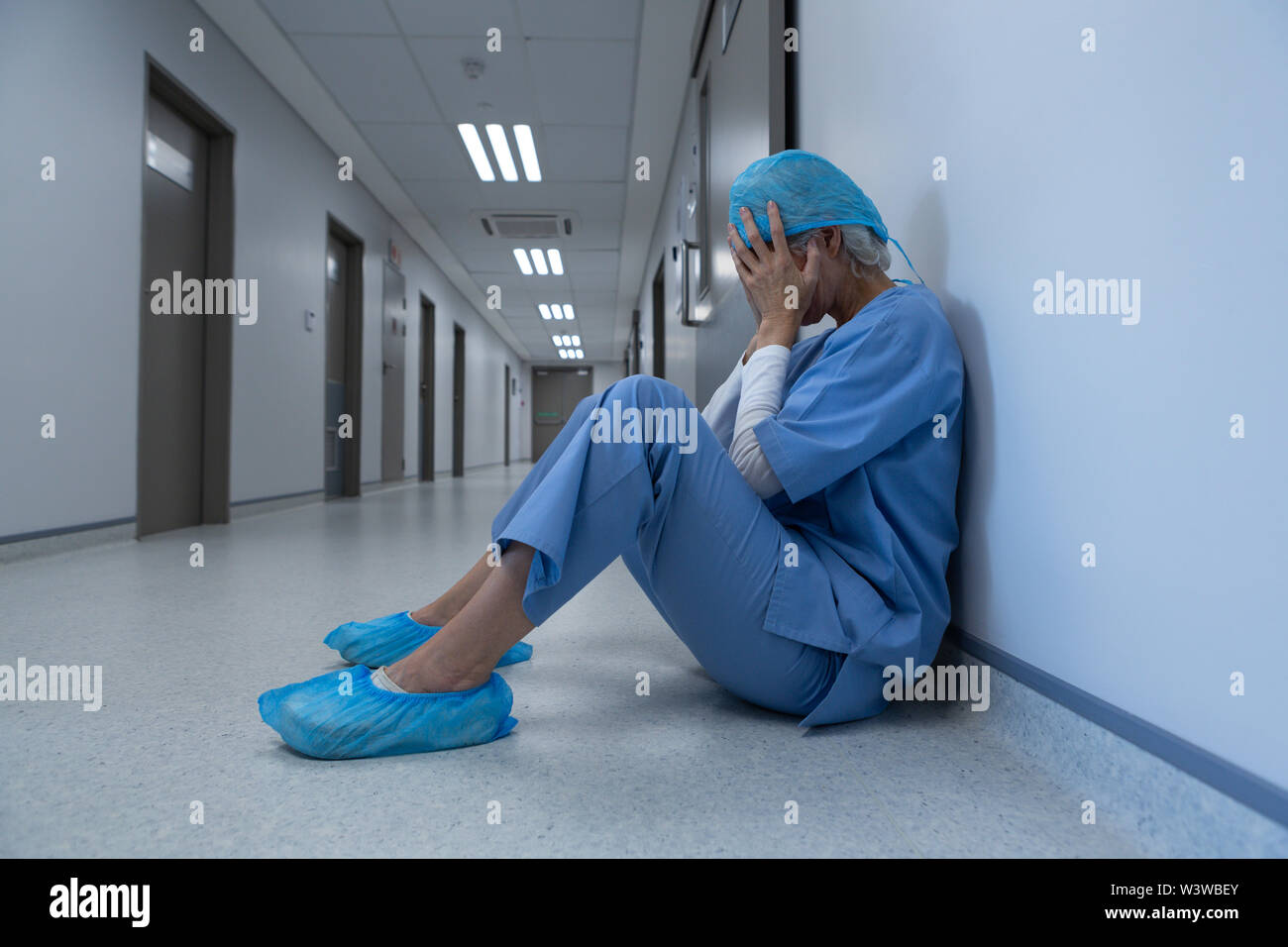 Tensed female surgeon covering her face in the corridor of hospital ...