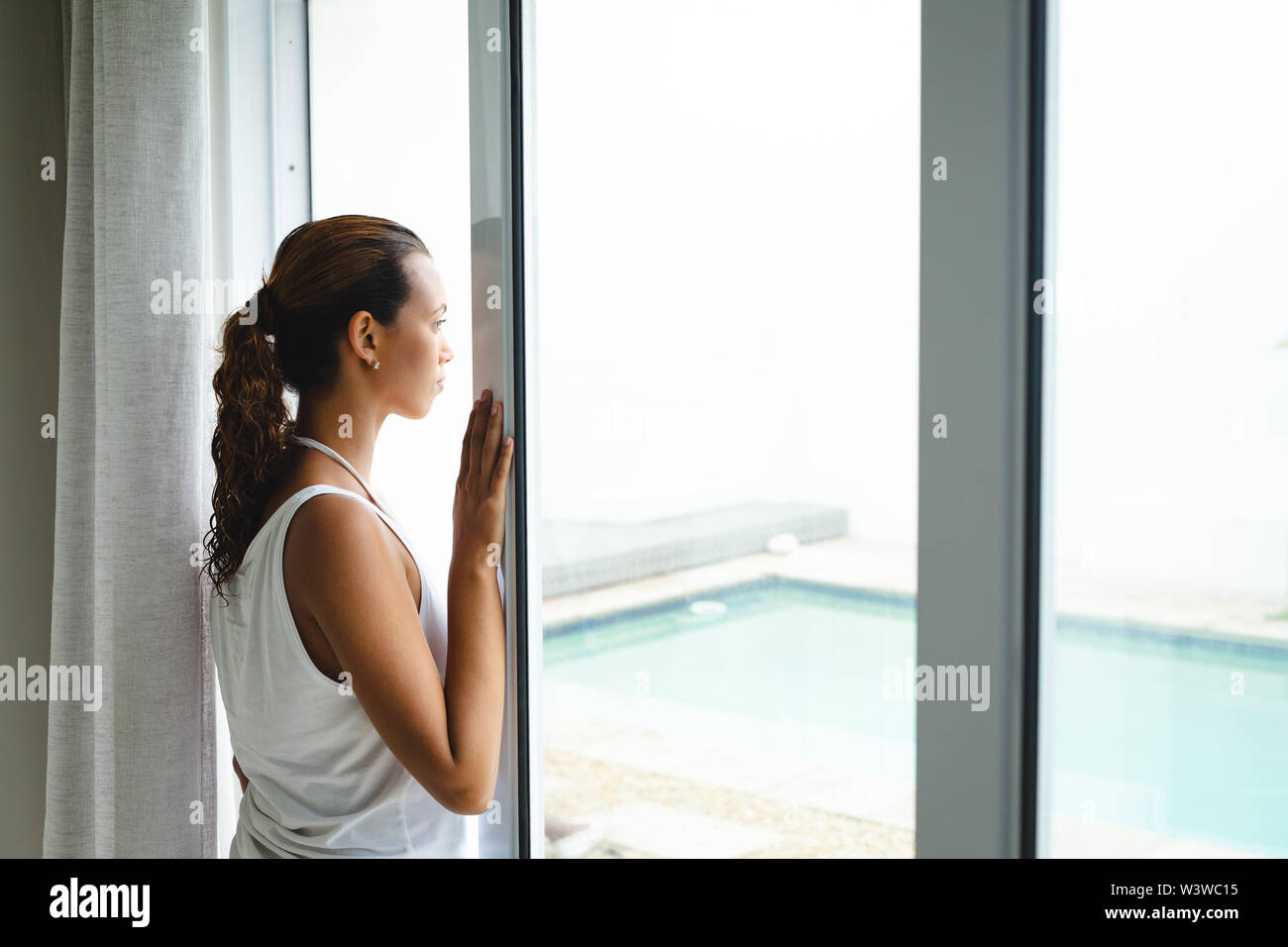 Woman looking through window in living room at home Stock Photo - Alamy