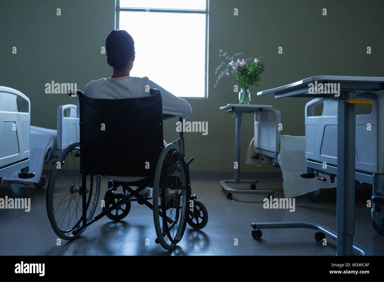 Patient looking through window while sitting in wheelchair in hospital ...