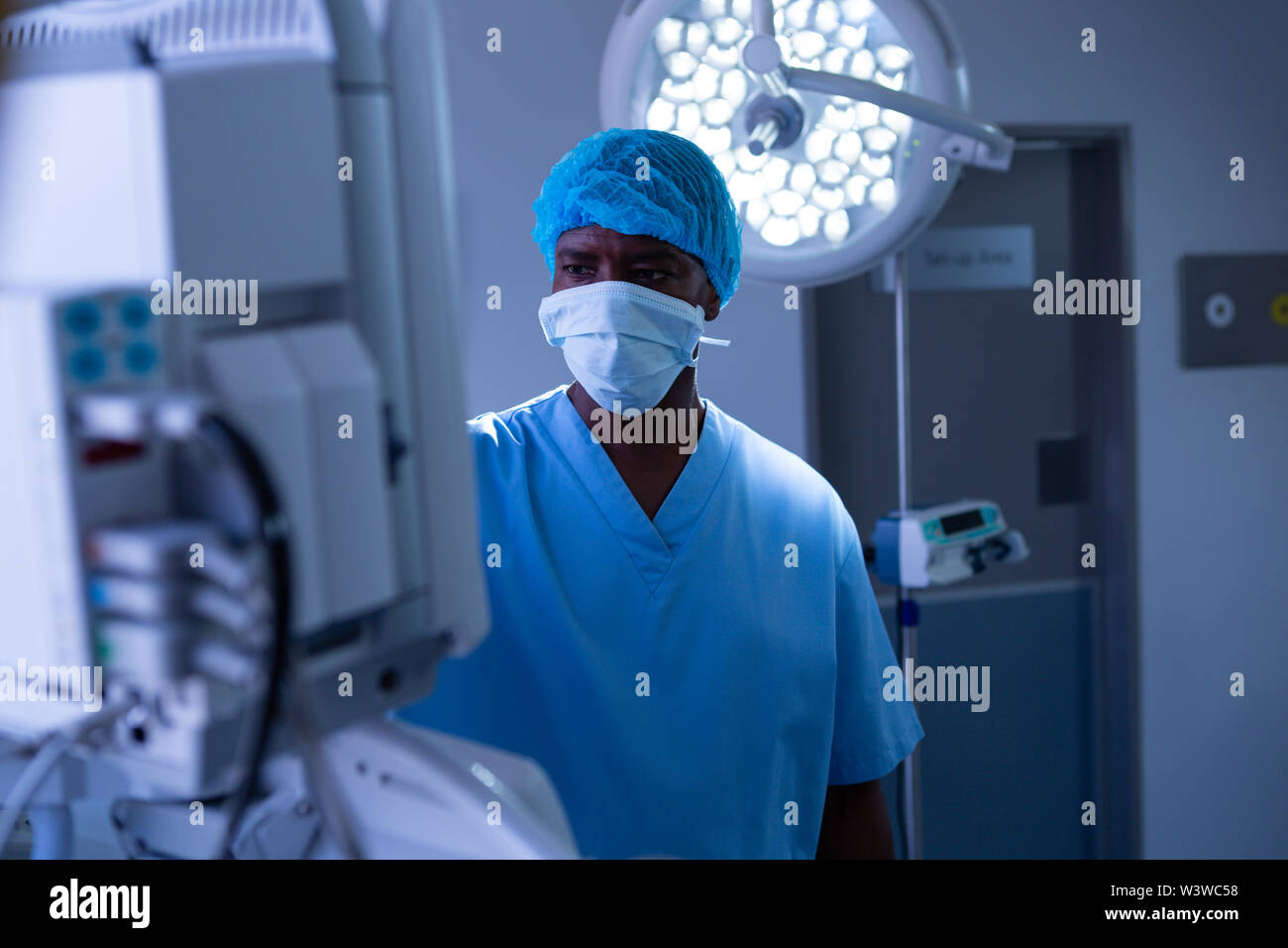 Male surgeon with surgical mask standing in operating room of hospital ...
