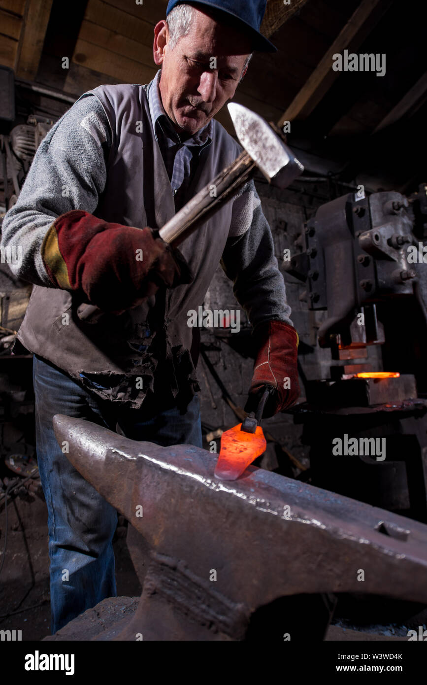 blacksmith manually forging the red hot molten metal on the anvil in ...