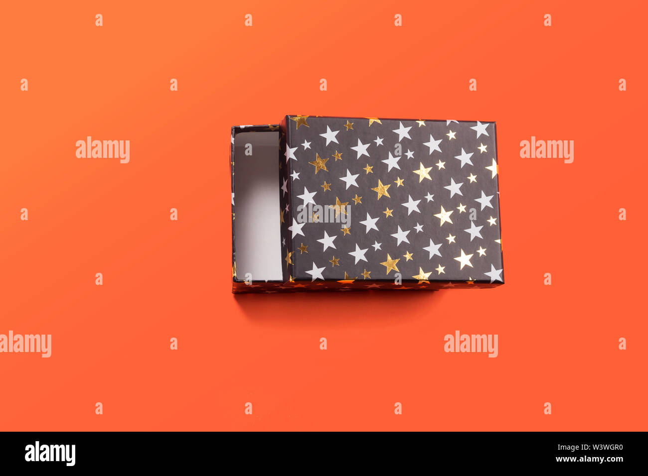 Black half open gift box with golden stars on orange coral background ...