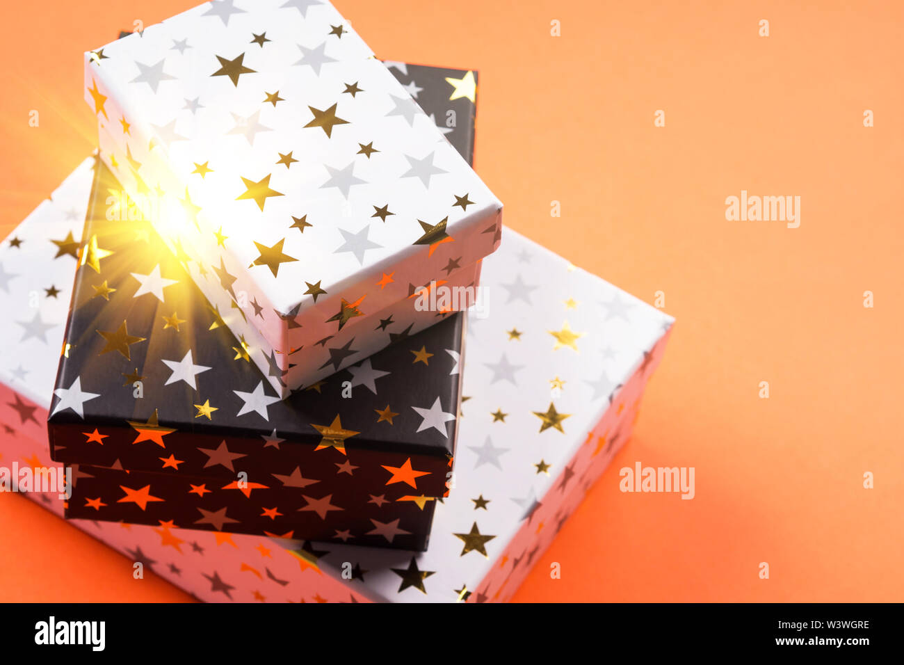 Stacked gift boxes with golden stars on orange background. Magic light ...