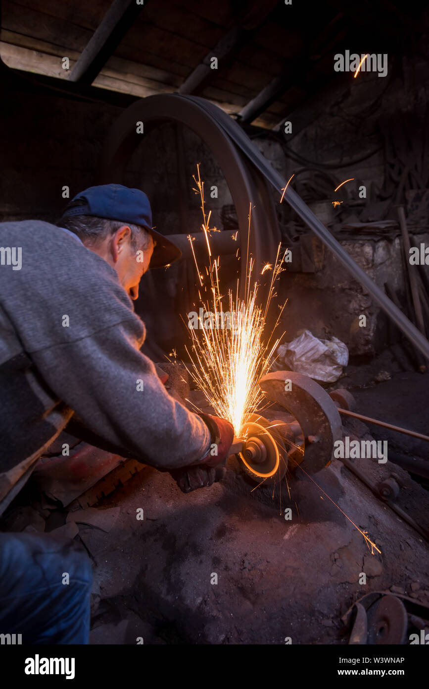 the blacksmith polishing metal products making sparks while using a ...
