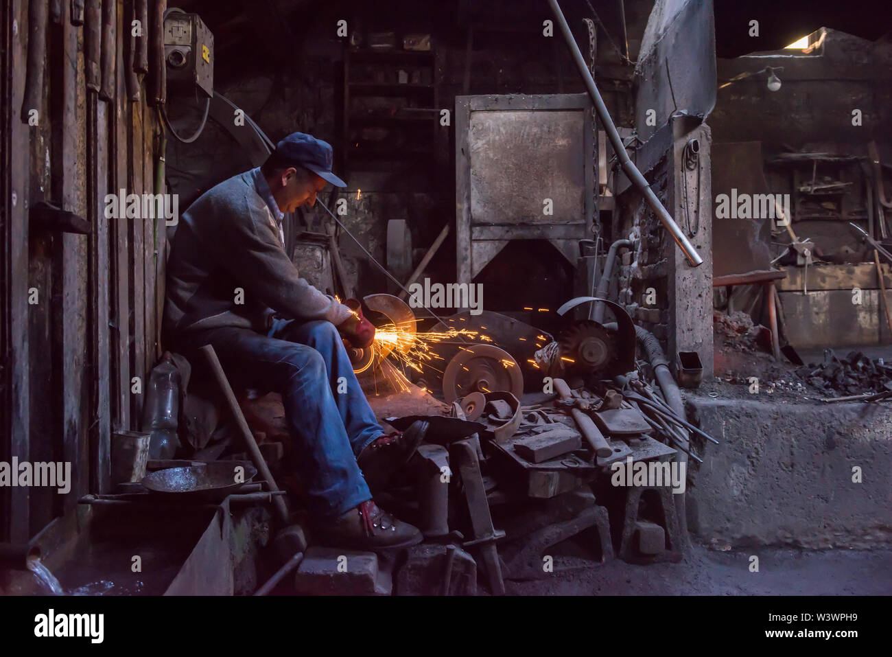 the blacksmith polishing metal products making sparks while using a ...