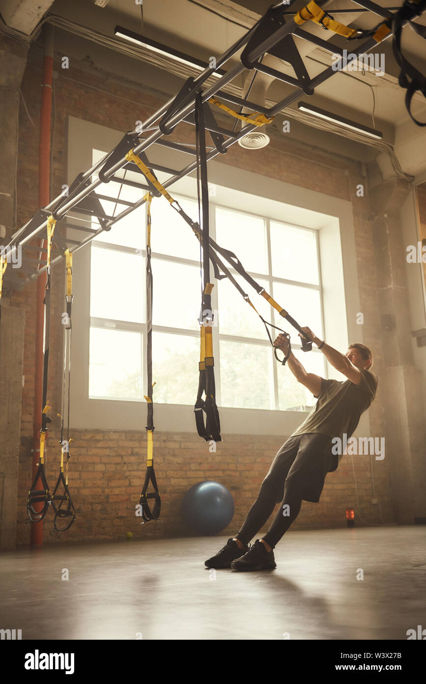 Strong athletic man training his arms with trx fitness straps at gym ...
