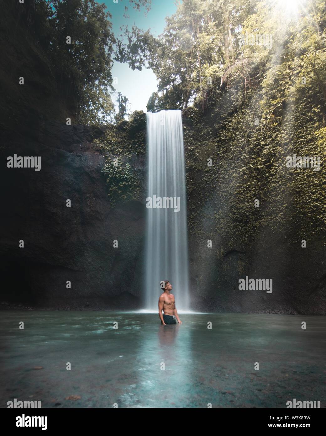 Fit male standing in a lake near a beautiful waterfall behind and ...