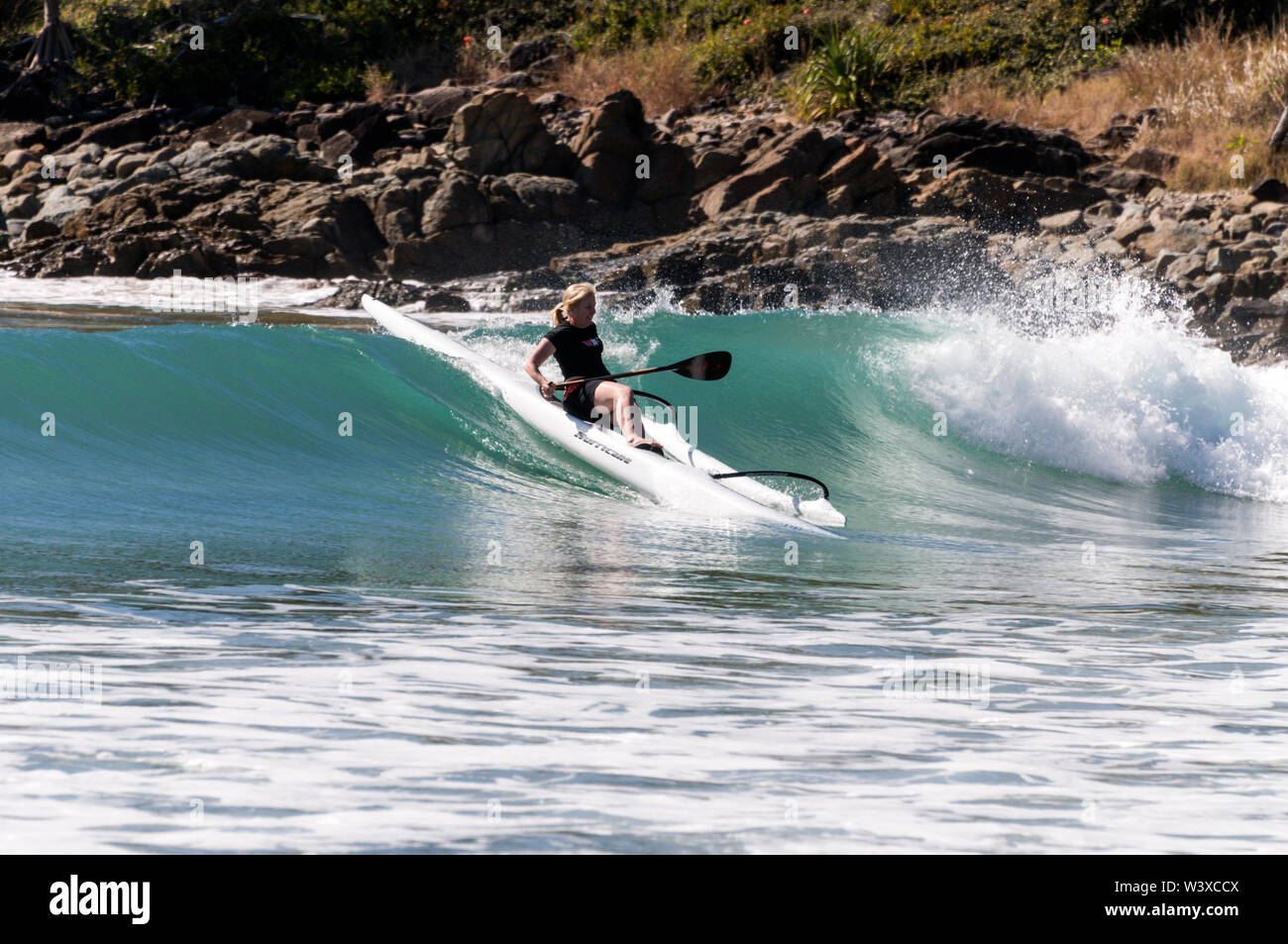 A young Australian woman riding the surf in her kayak in the Coral Sea ...