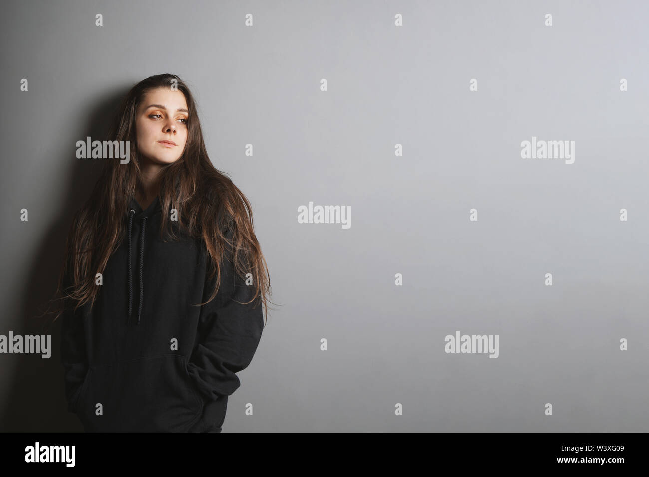 sad young goth woman wearing black sweater leaning against wall with ...