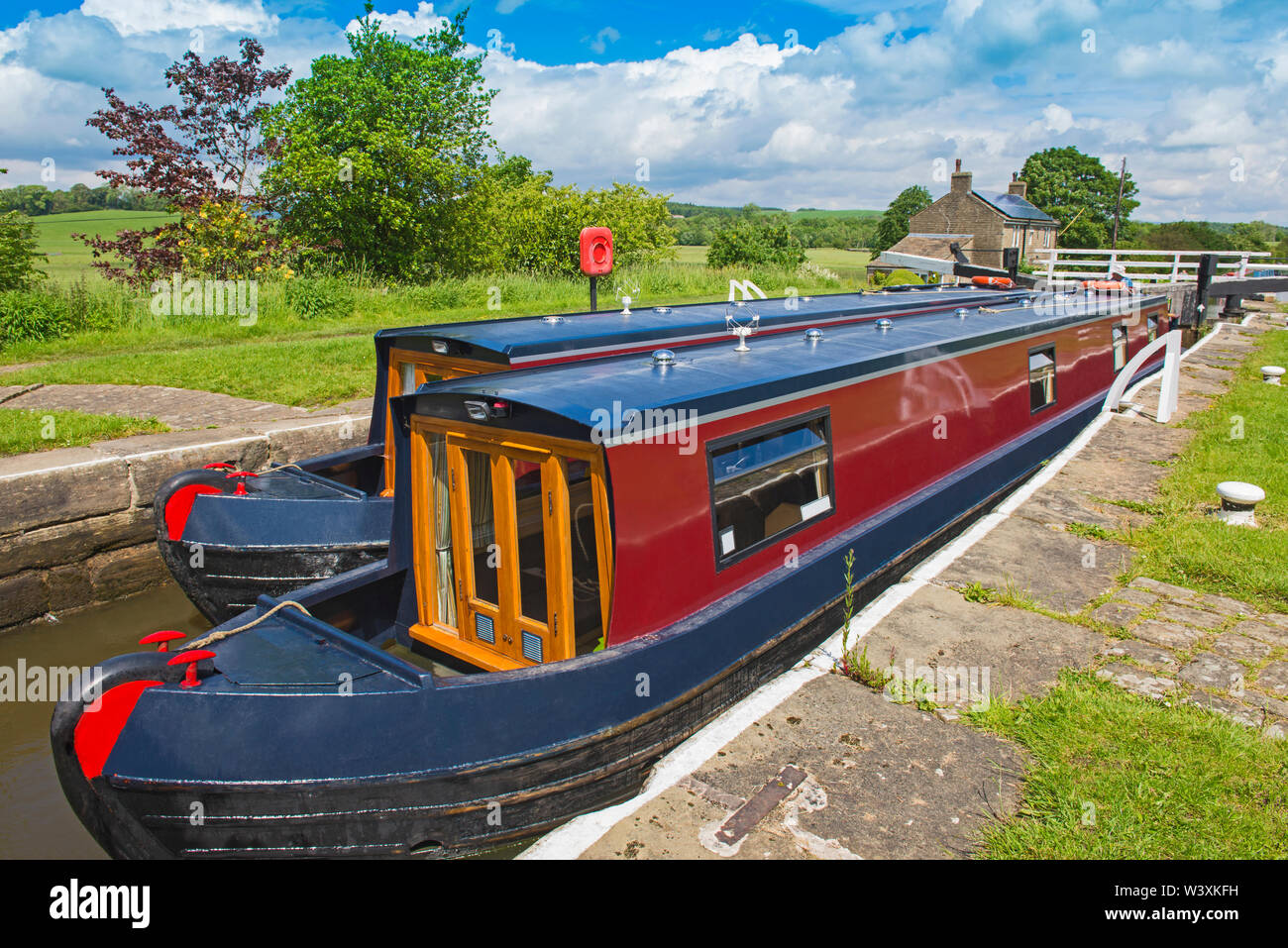 Two narrowboats traveling through a lock in English rural countryside ...