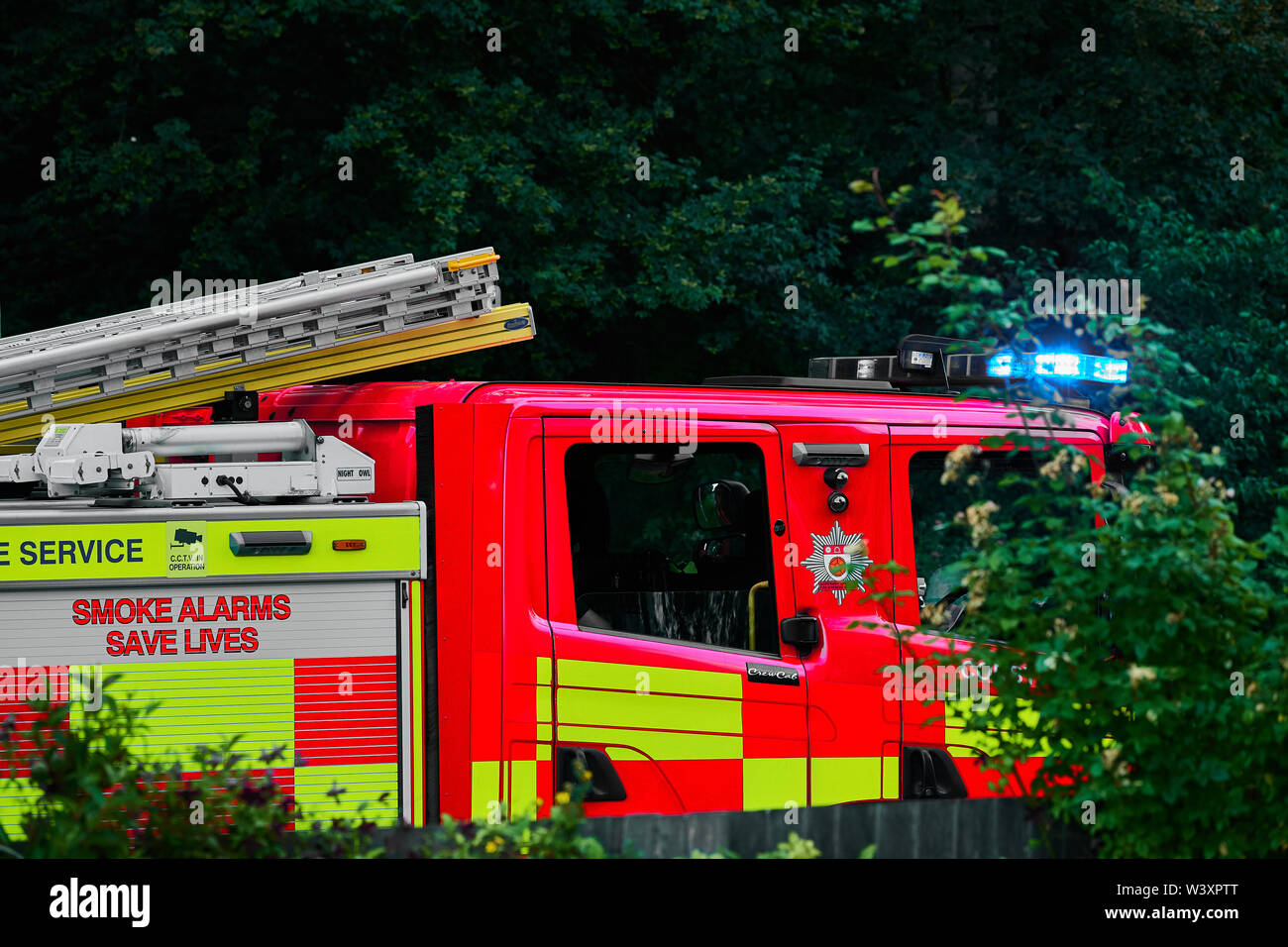 Red fire engine with blue flashing light stopped outside a woodland ...