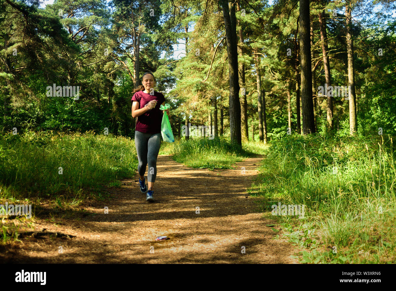 Woman jogging with garbage bag in forest. Collecting trash. Plogging ...
