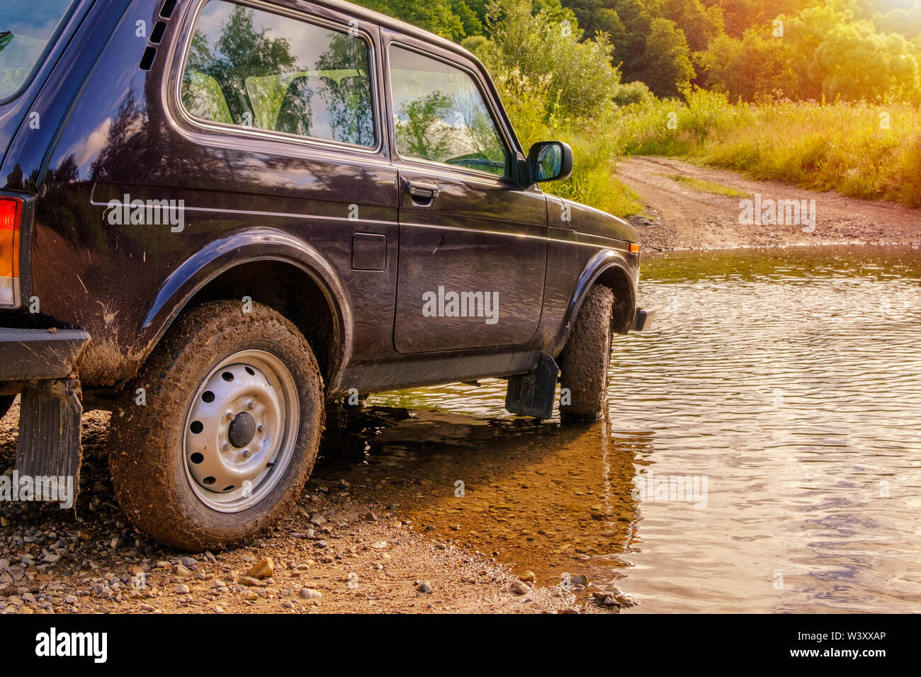 Off-road vehicle at a ford across the river in the glowing light of ...