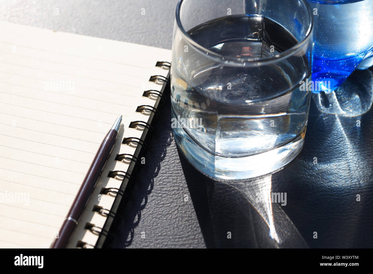 Glass of water near pen lying on open notepad Stock Photo - Alamy