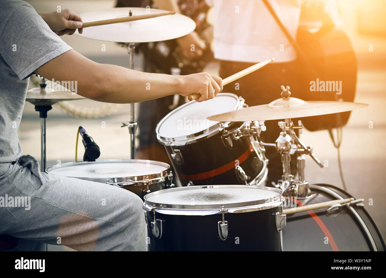 The drummer in gray clothes plays on a black and red drum set with ...