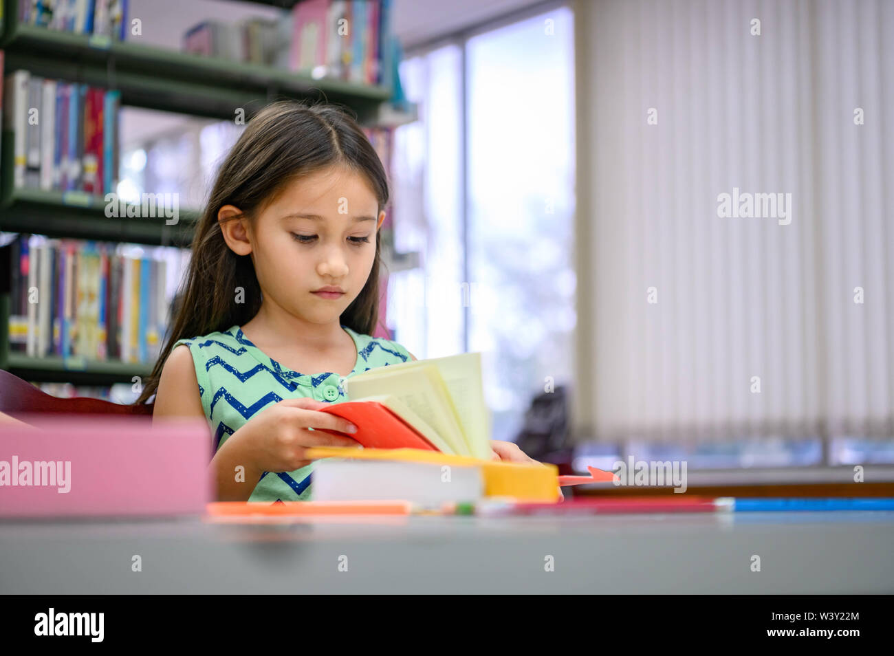 Cute little girl reading books in library attentively at school. Girl ...