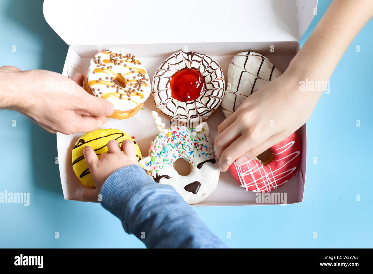 People hands takes donuts from donuts box over blue background. Family ...