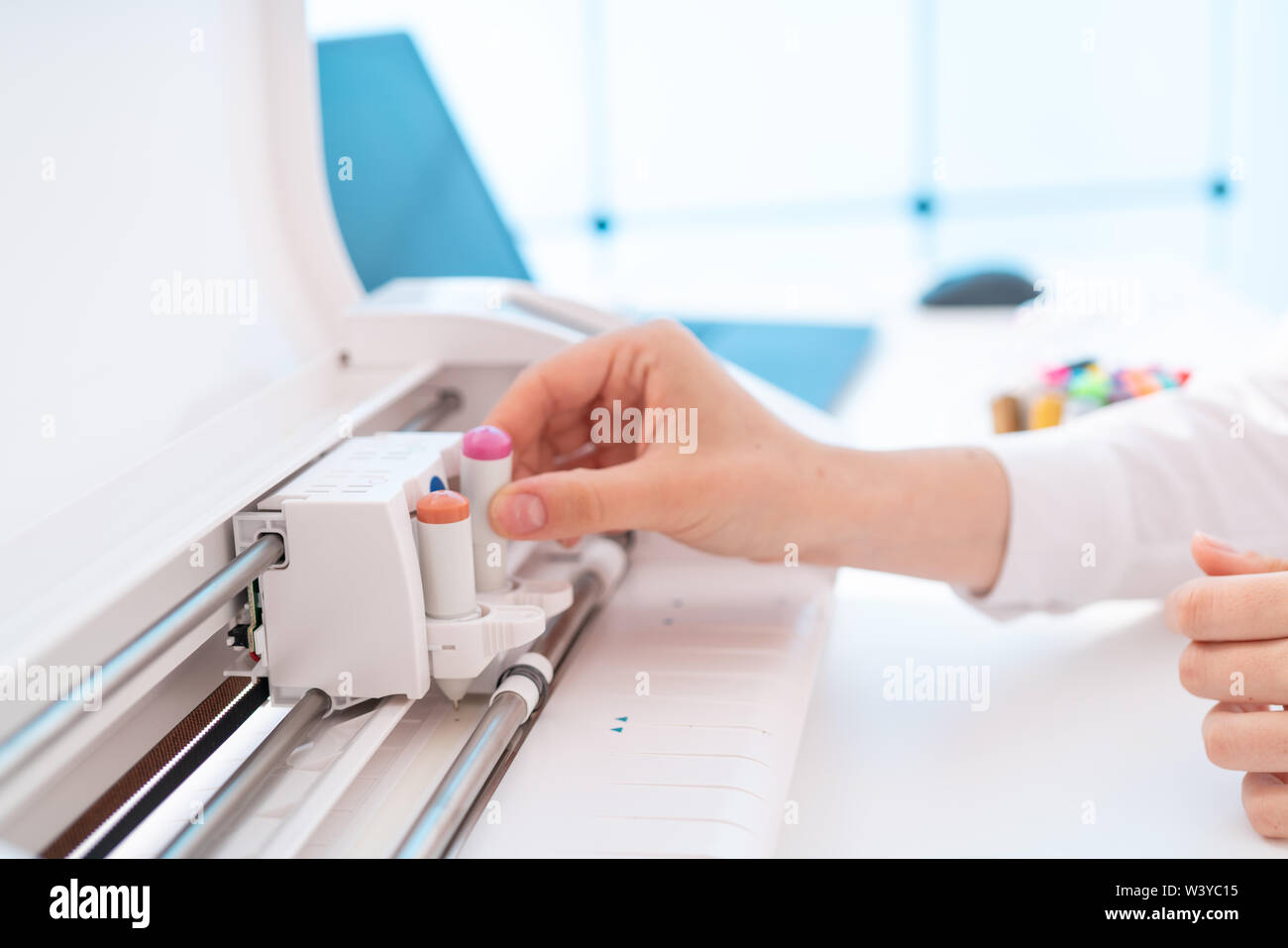 Young woman in printing office insert paper and color pens on plotter ...