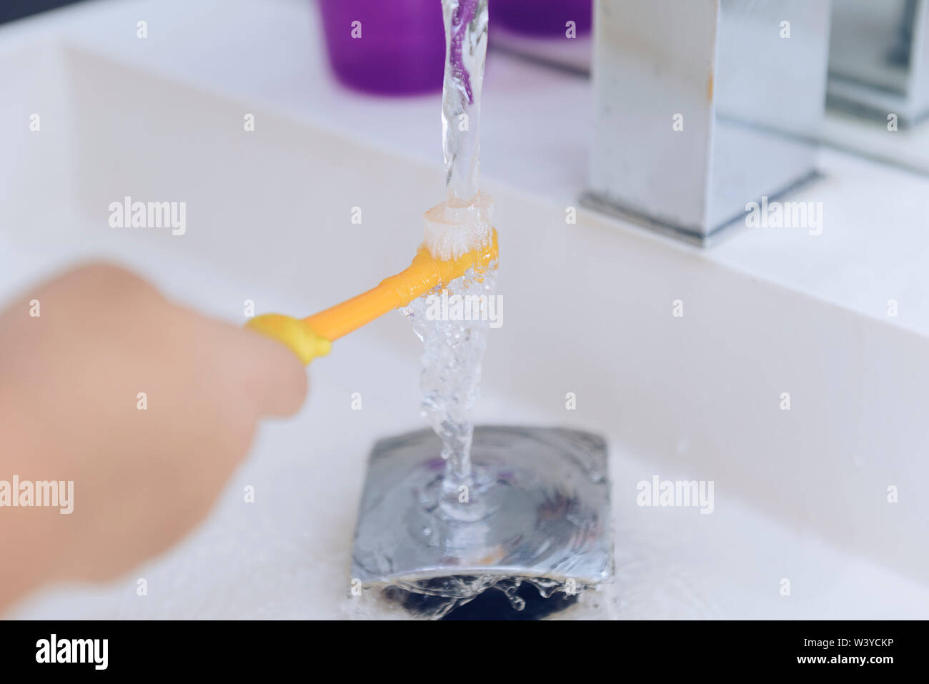hand of a kid wetting the toothbrush, after taking a shower she ...