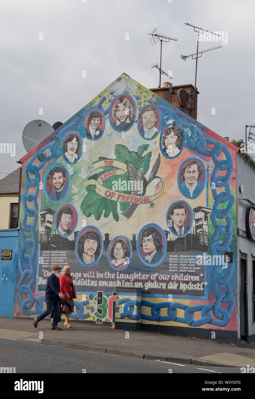 Couple walking past Republican murals in the Bogside area of Derry ...