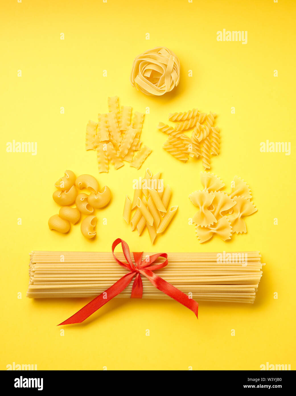 A christmas tree made with various forms of pasta on yellow background ...
