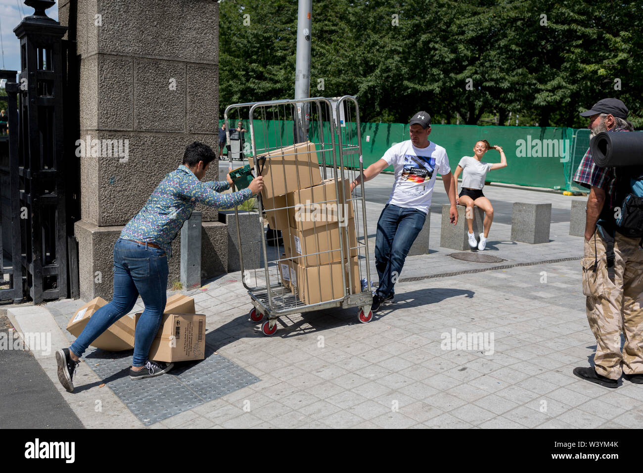 As a young woman poses for photos on the Southbank, deliverymen push a ...