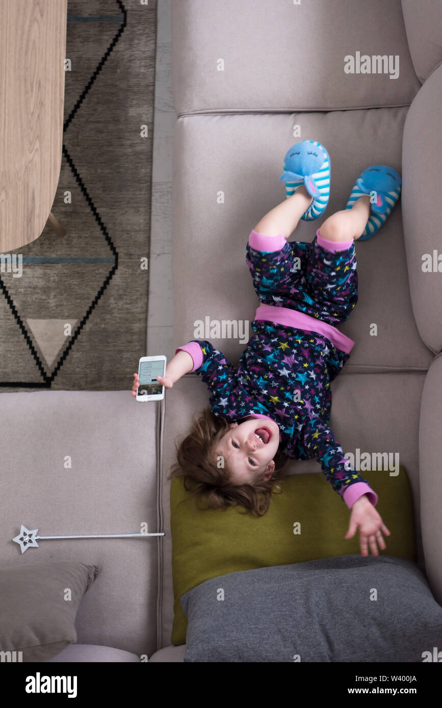 top view of cute little girl using a smartphone and smiling while lying ...