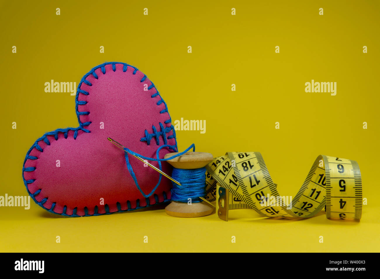 Hand stitched fabric heart and spool of thread with needle on yellow ...