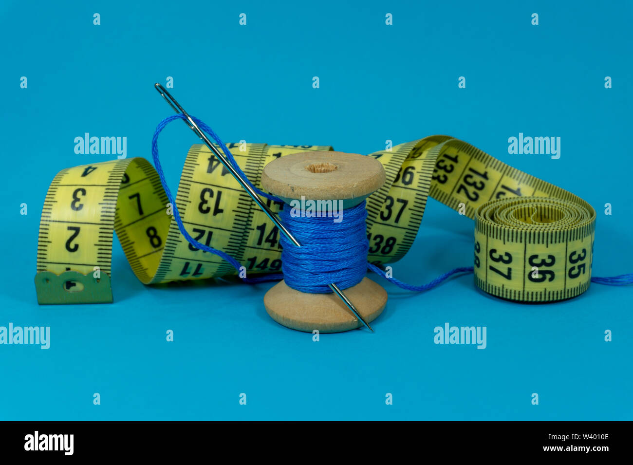 A close up image of a tape measure, spool of blue thread and sewing ...