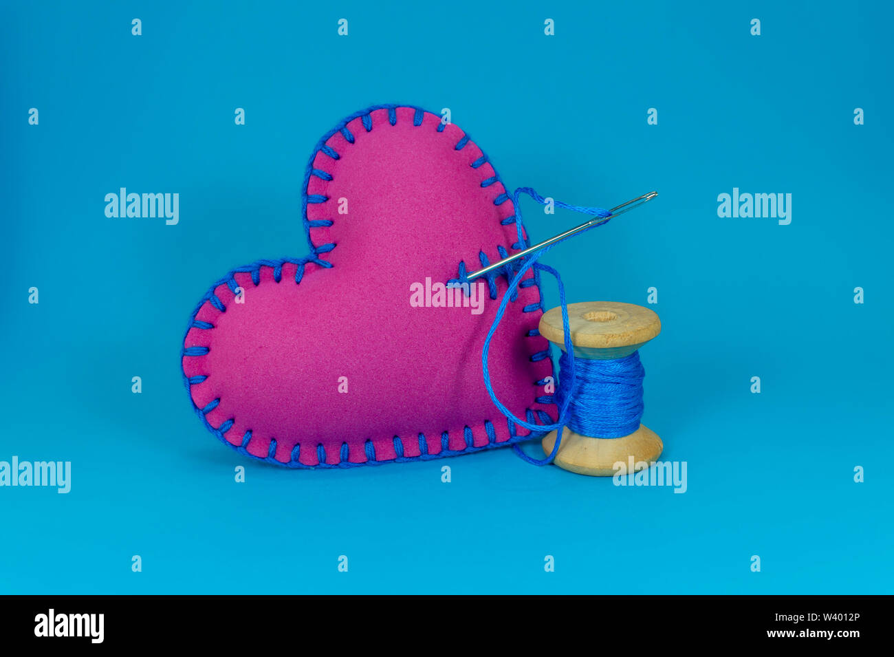 Hand stitched fabric heart and spool of thread with needle on blue ...