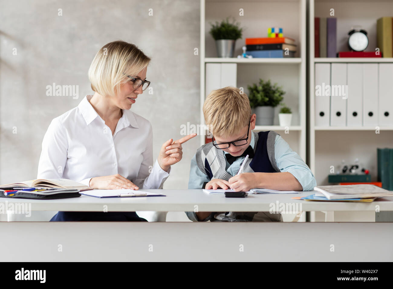A young student and his confident-looking teacher sit at the table and ...