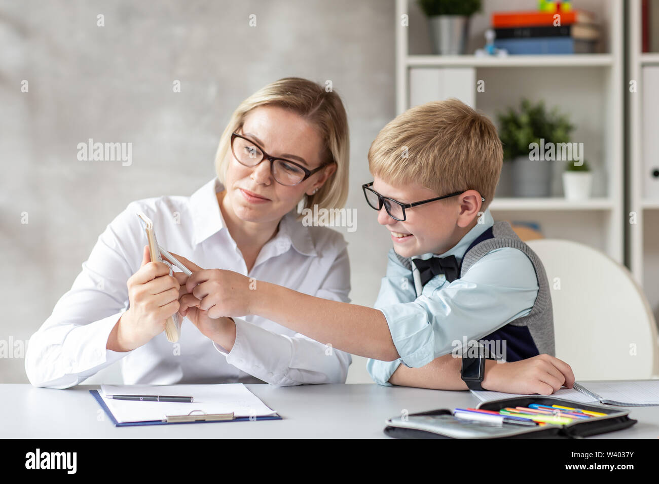 Smiling boy showing something to his cute teacher in her manual Stock ...