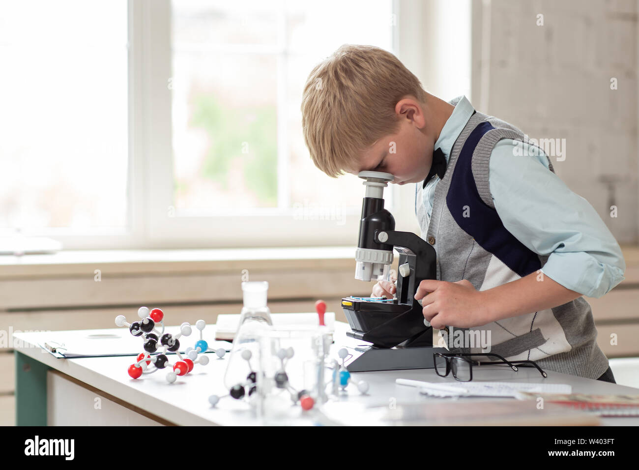 A young boy in a white shirt and sweater examines the sample under a ...