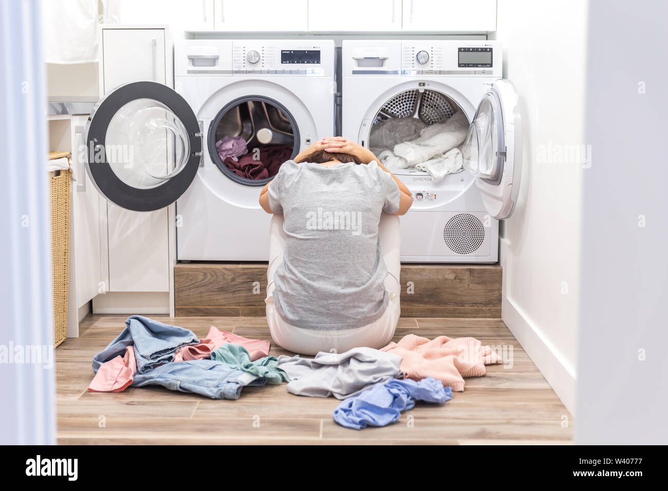 Young Tired sad Woman sitting on the floor in laundry room, back view ...